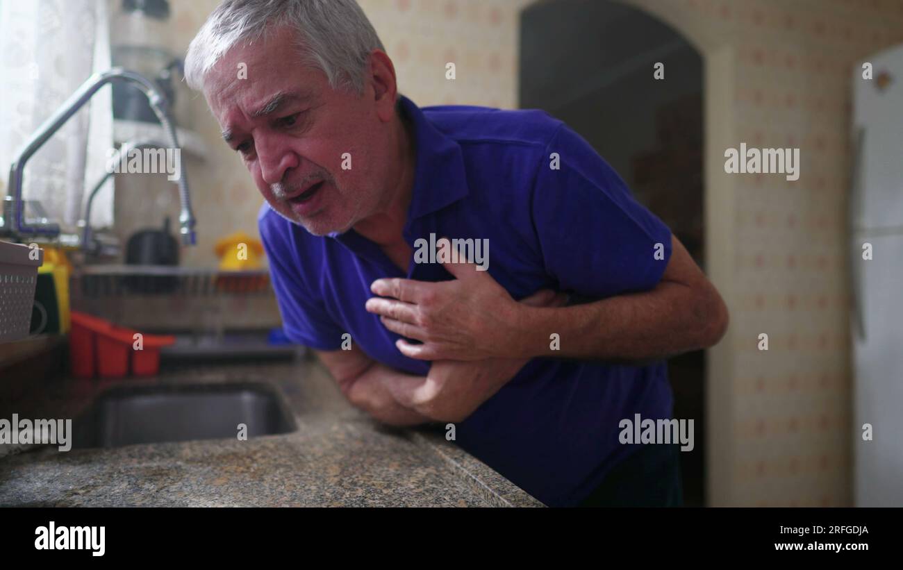 Senior man suffering heart attack alone at home leaning on kitchen sink ...