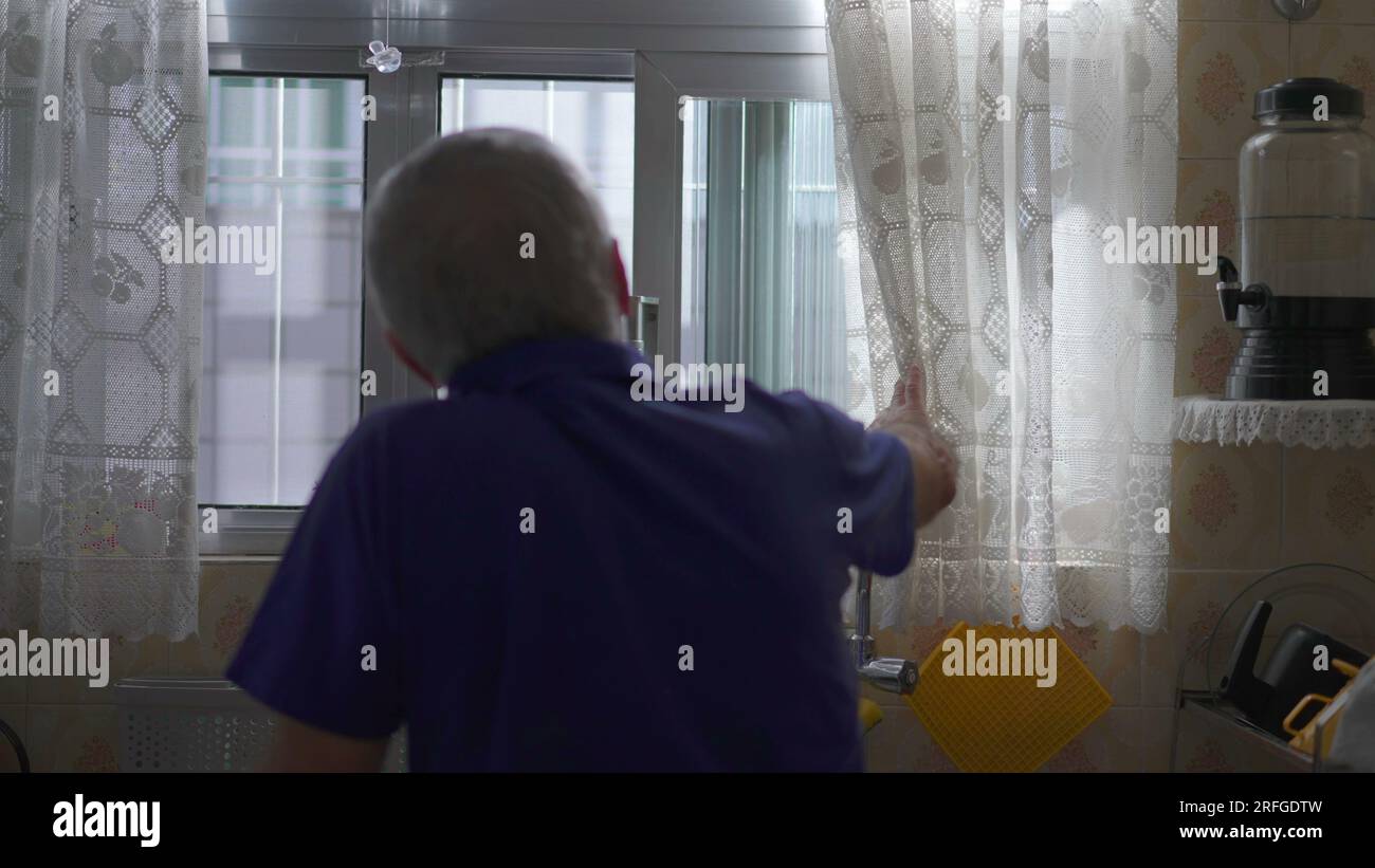 Back of elderly man looking out window view at home, opening curtains ...