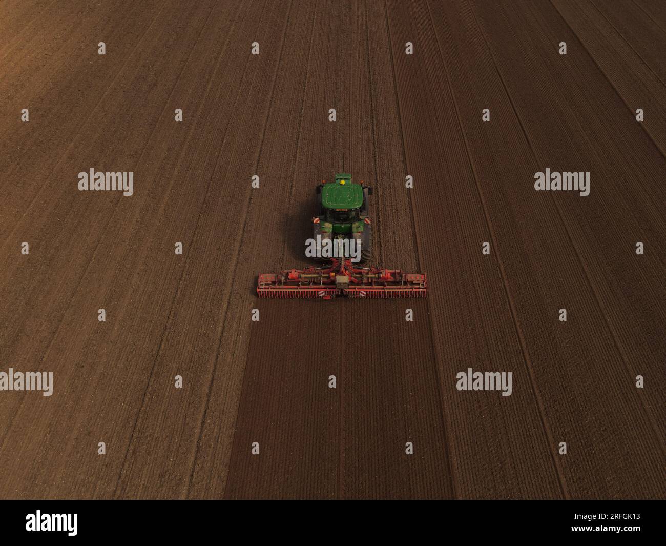 A John Deere tractor, seen from above, cultivates a field in ...