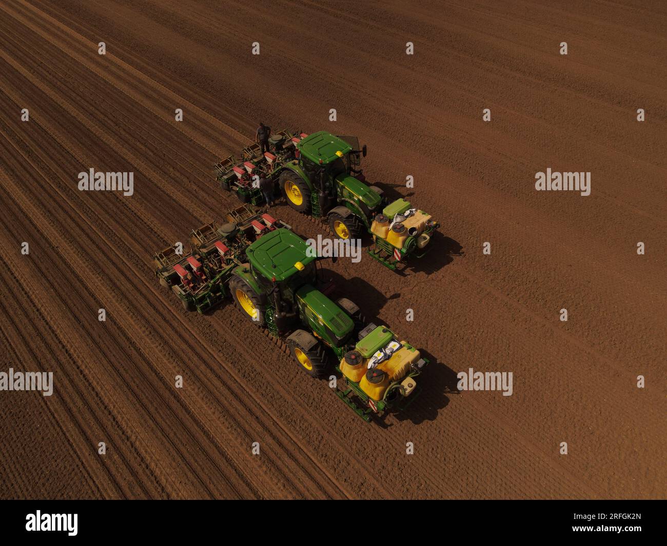 Two John Deere tractors, seen from above, work together to plant a ...