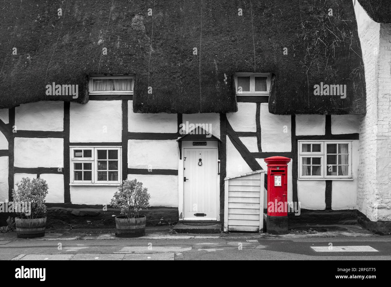 Thatched cottage with red postbox letterbox, monochrome with colour ...