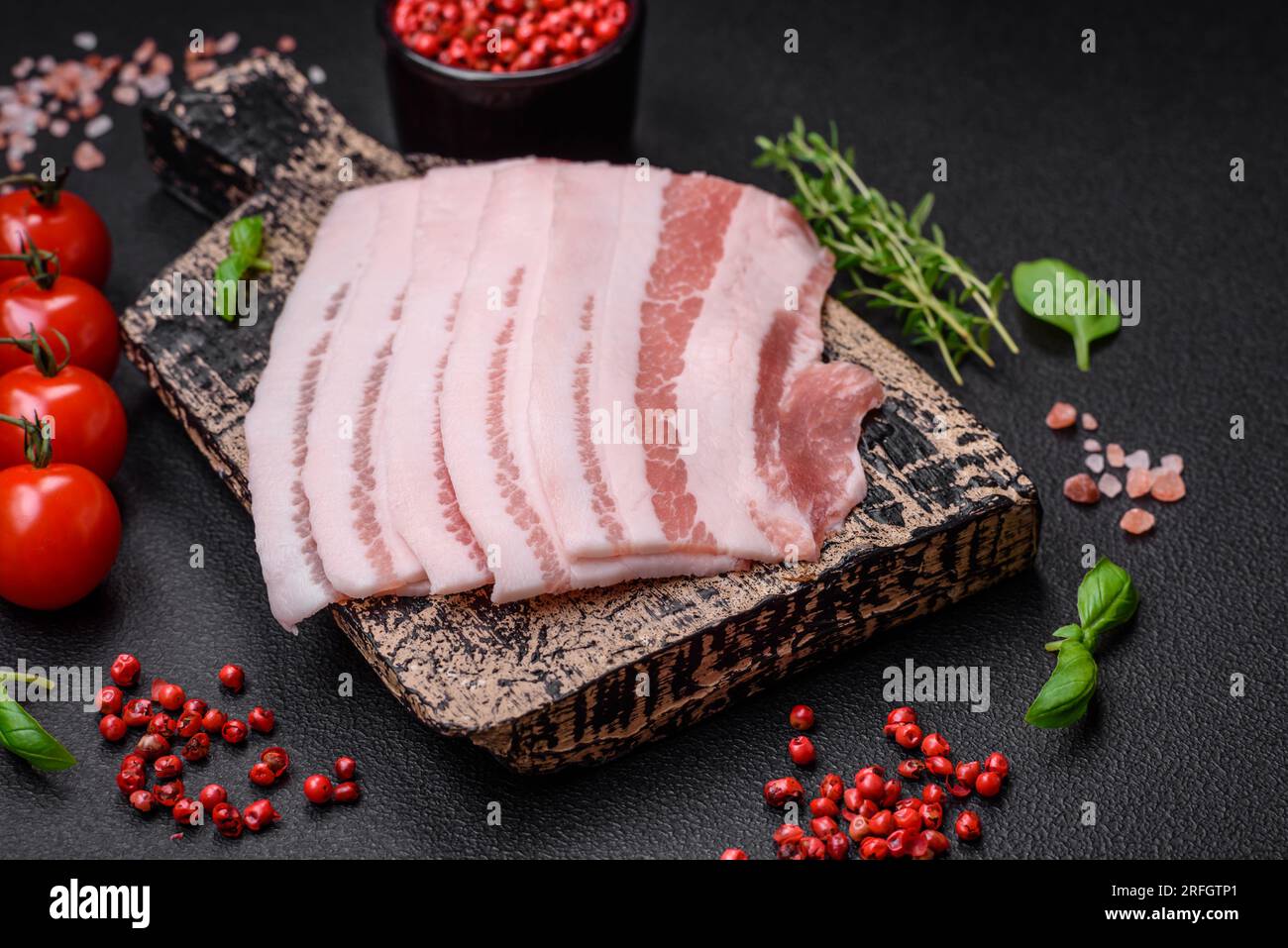 Fresh raw bacon cut into slices with salt, spices and herbs on a dark ...