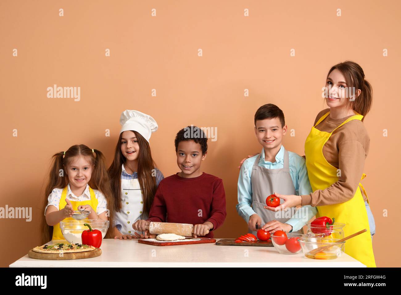 Female chef with group of little children during cooking class on beige ...
