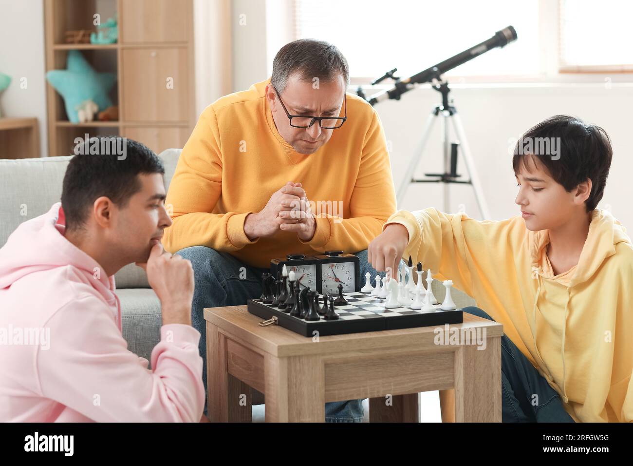 Happy little boy with his dad and grandfather playing chess at home ...