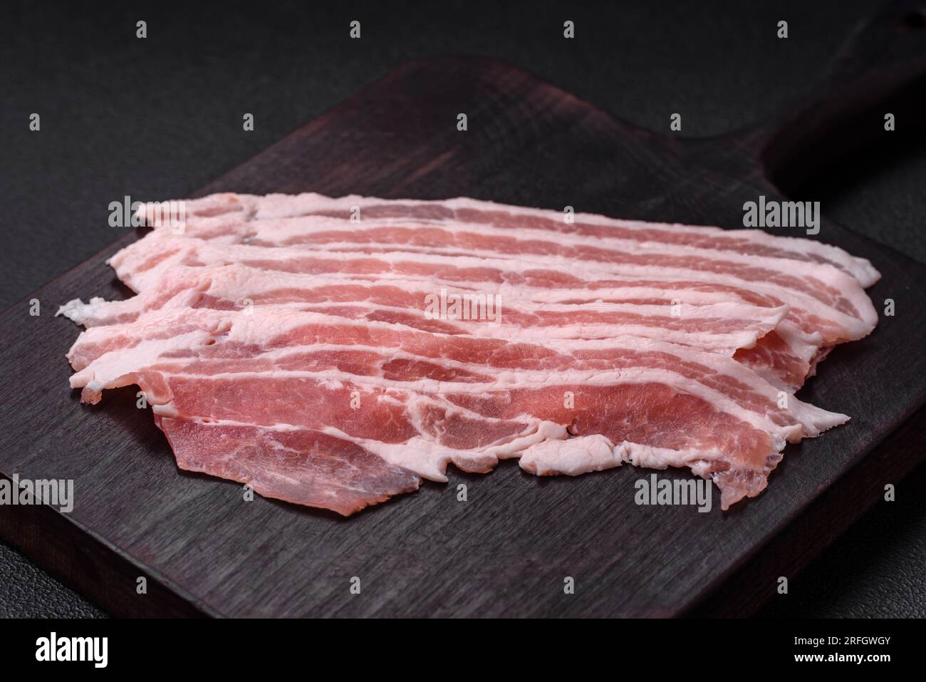 Fresh raw bacon cut into slices with salt, spices and herbs on a dark ...