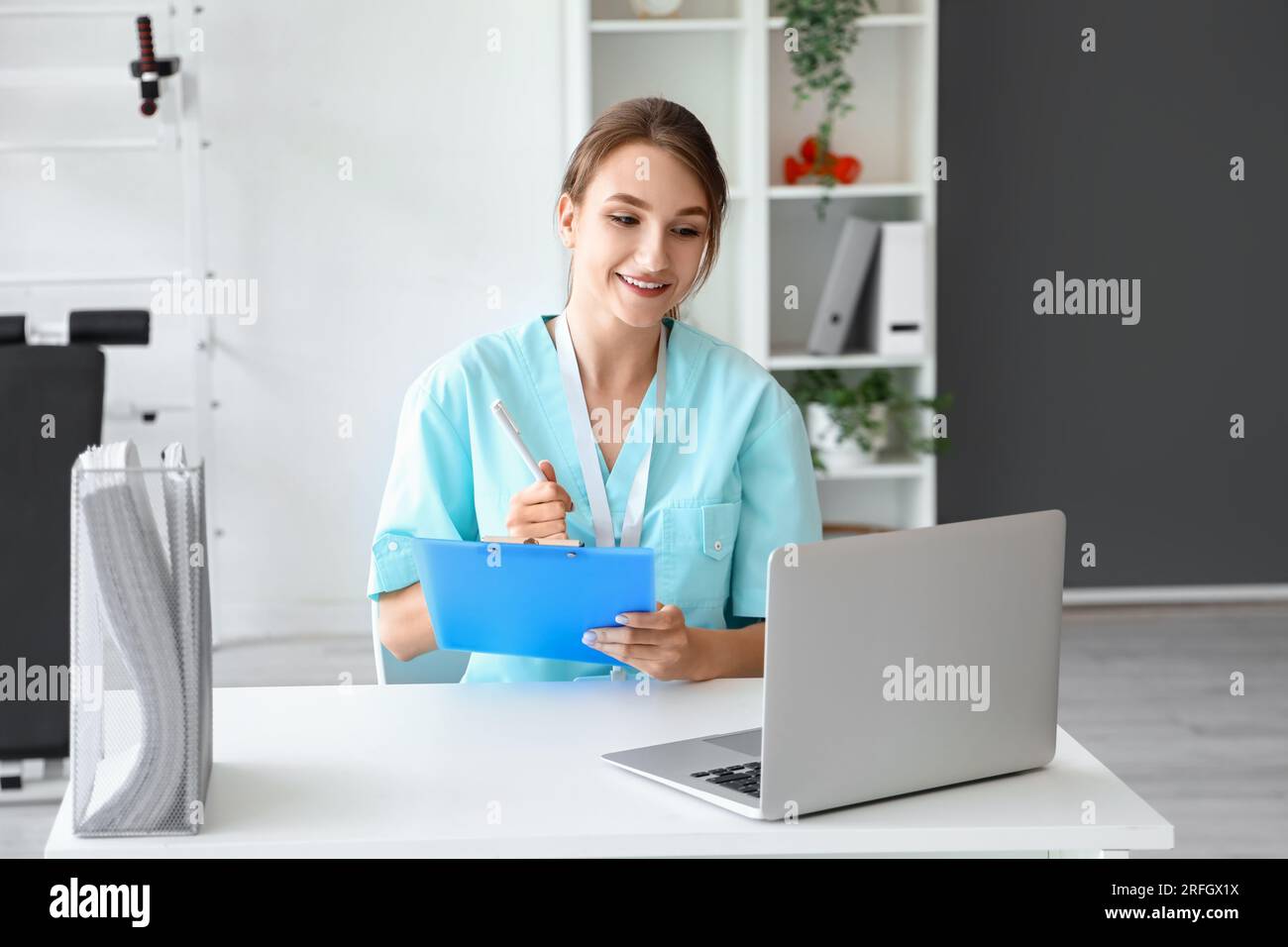 Female medical intern with clipboard using laptop at hospital Stock ...