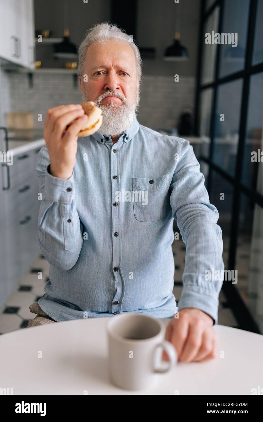 Vertical portrait of disgruntled mature adult male eating unappetizing ...