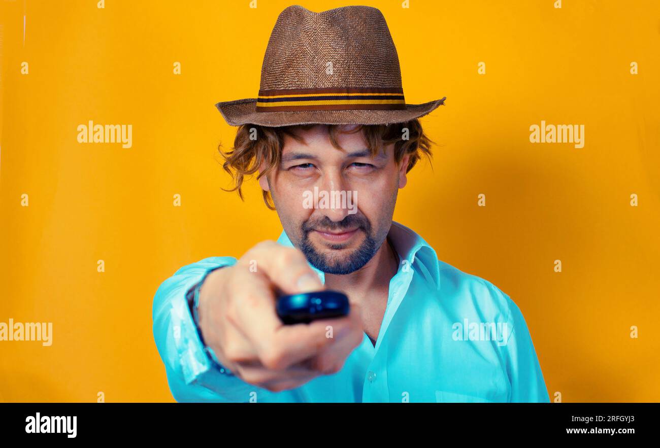 Expressive young man on a yellow background using a remote control ...