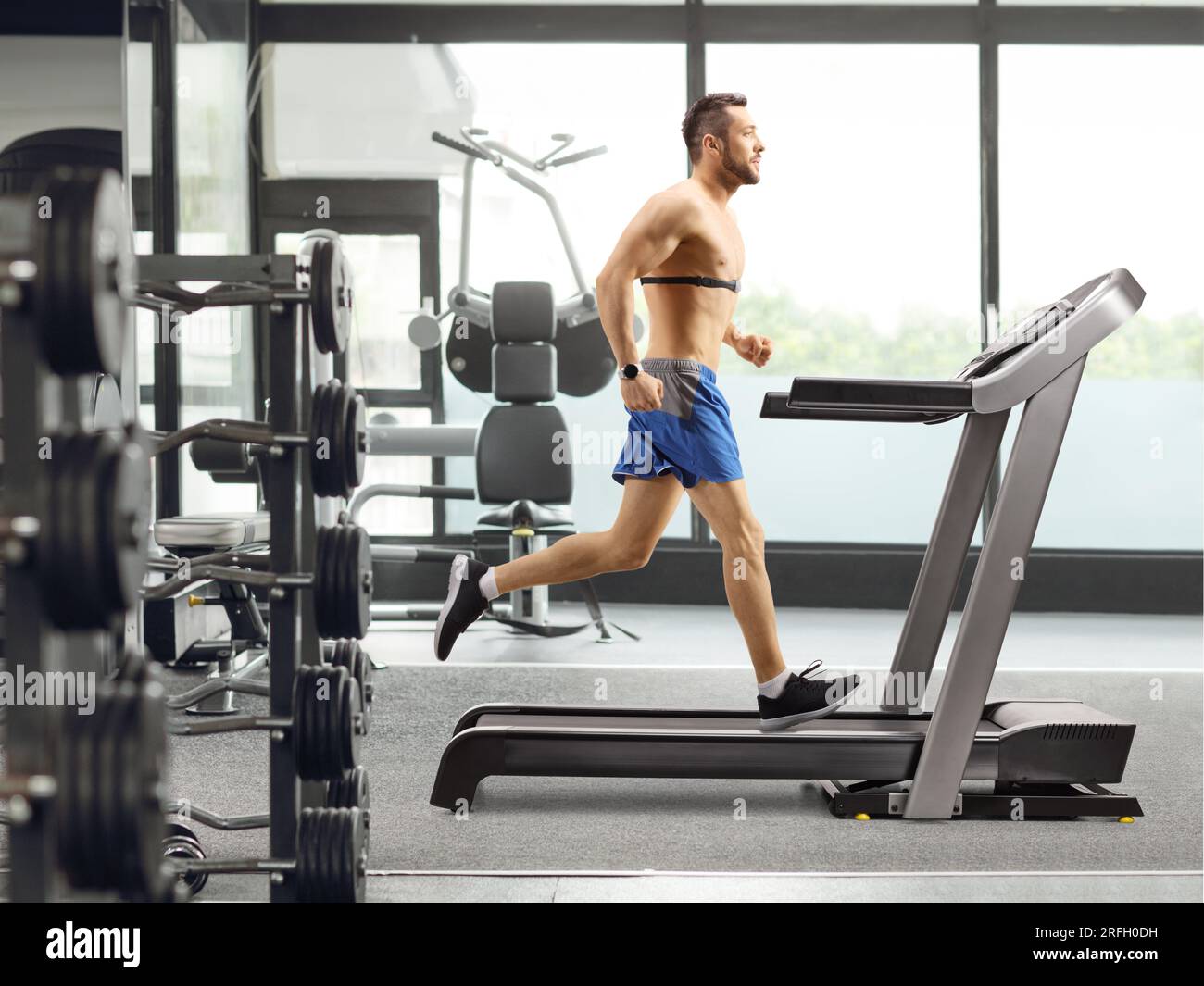 Full length profile shot of a man in a gym running on a treadmill with ...