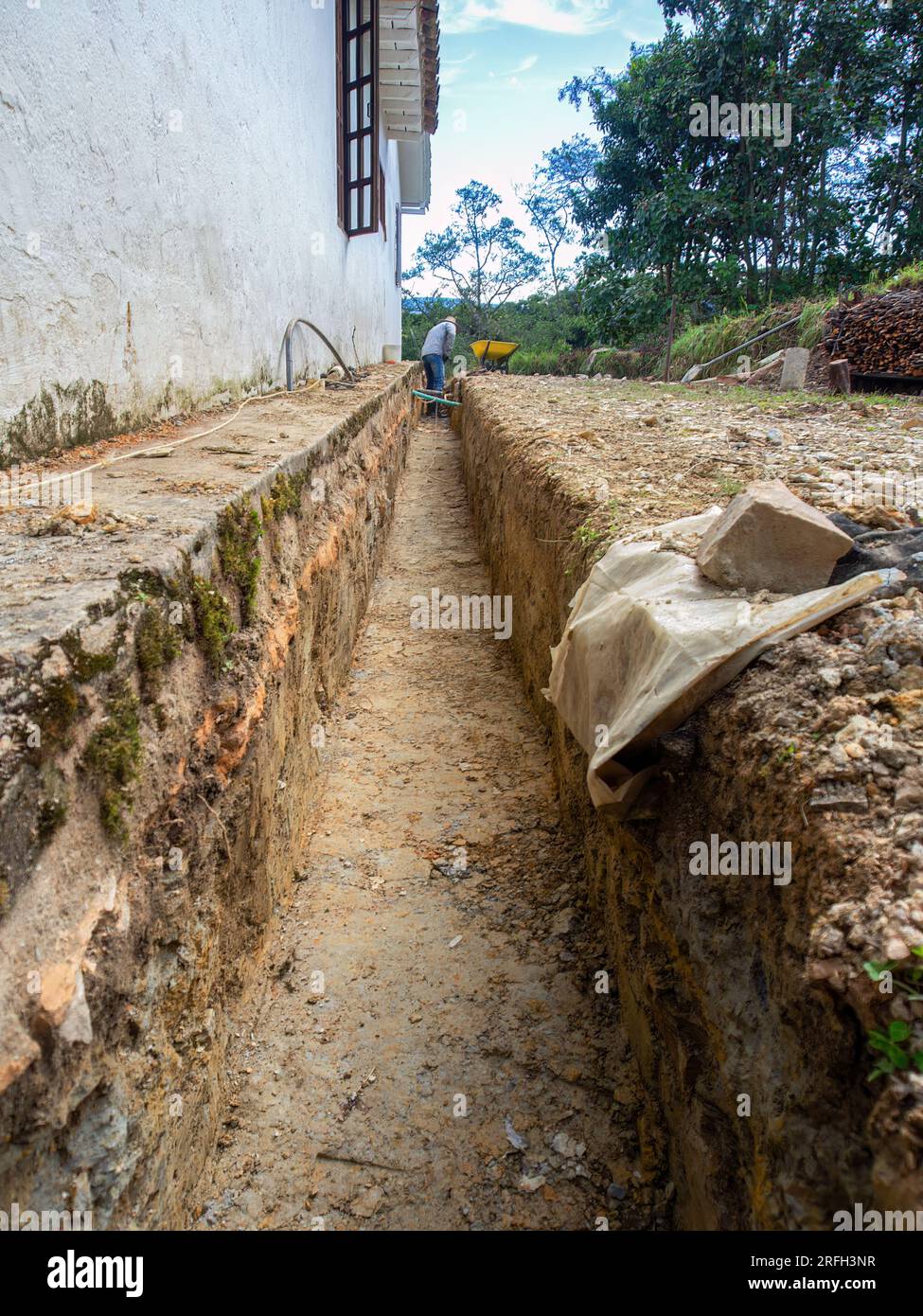 A man digging a ditch for rain water management in a farmhouse, in the ...