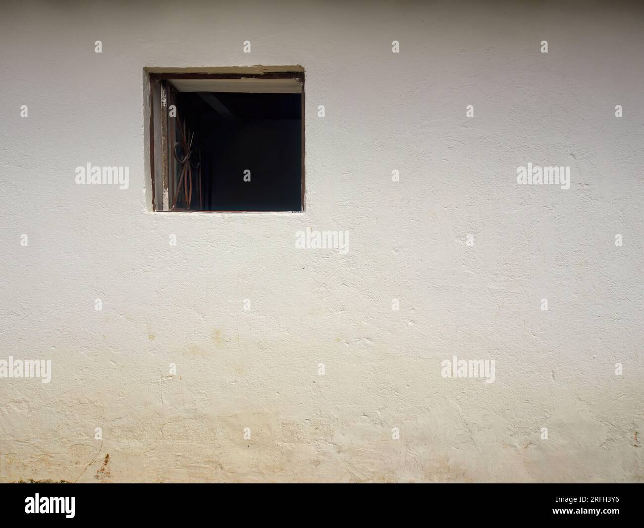 A little rustic open square window on a weathered white wall of a ...