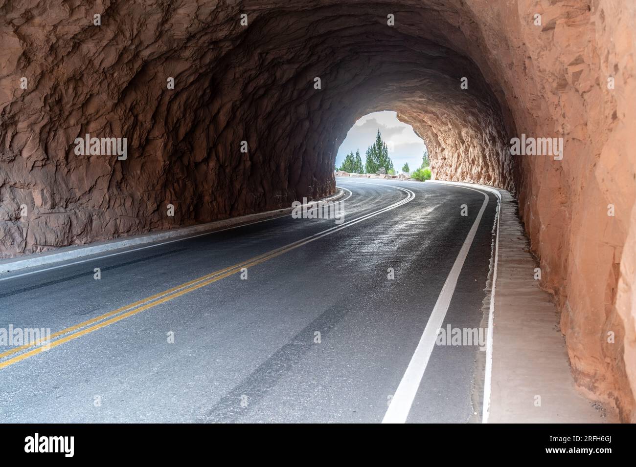 A two lane automobile tunnel cut into sandstone with a bend to the left ...