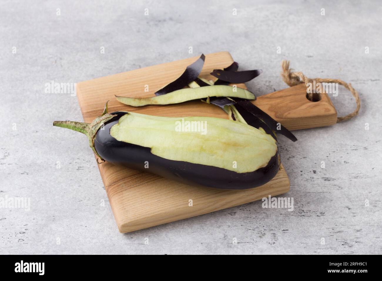 A whole eggplant with the skin removed on a wooden board on a gray ...