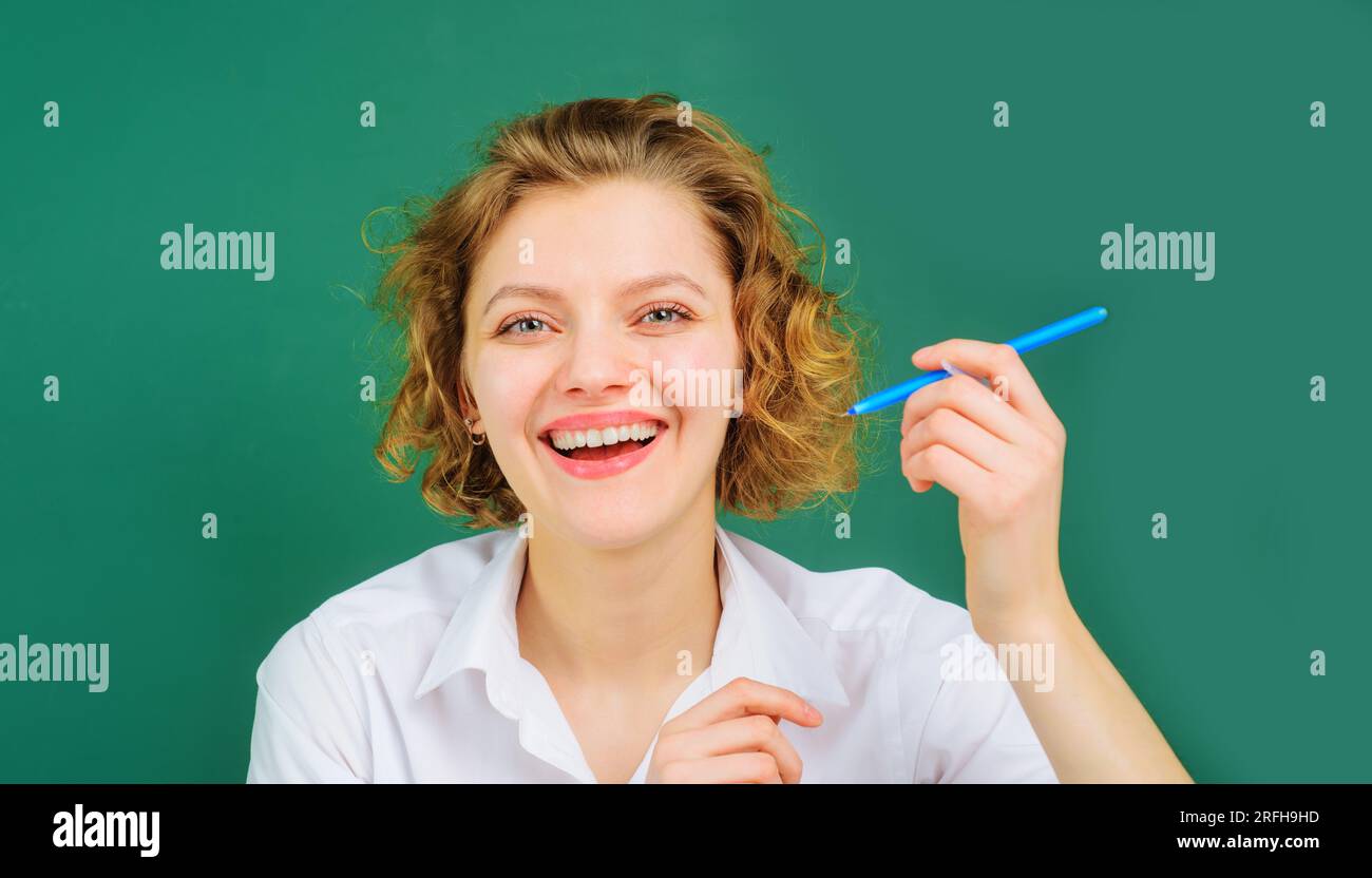 Smiling female teacher with pen in classroom. School supplies ...