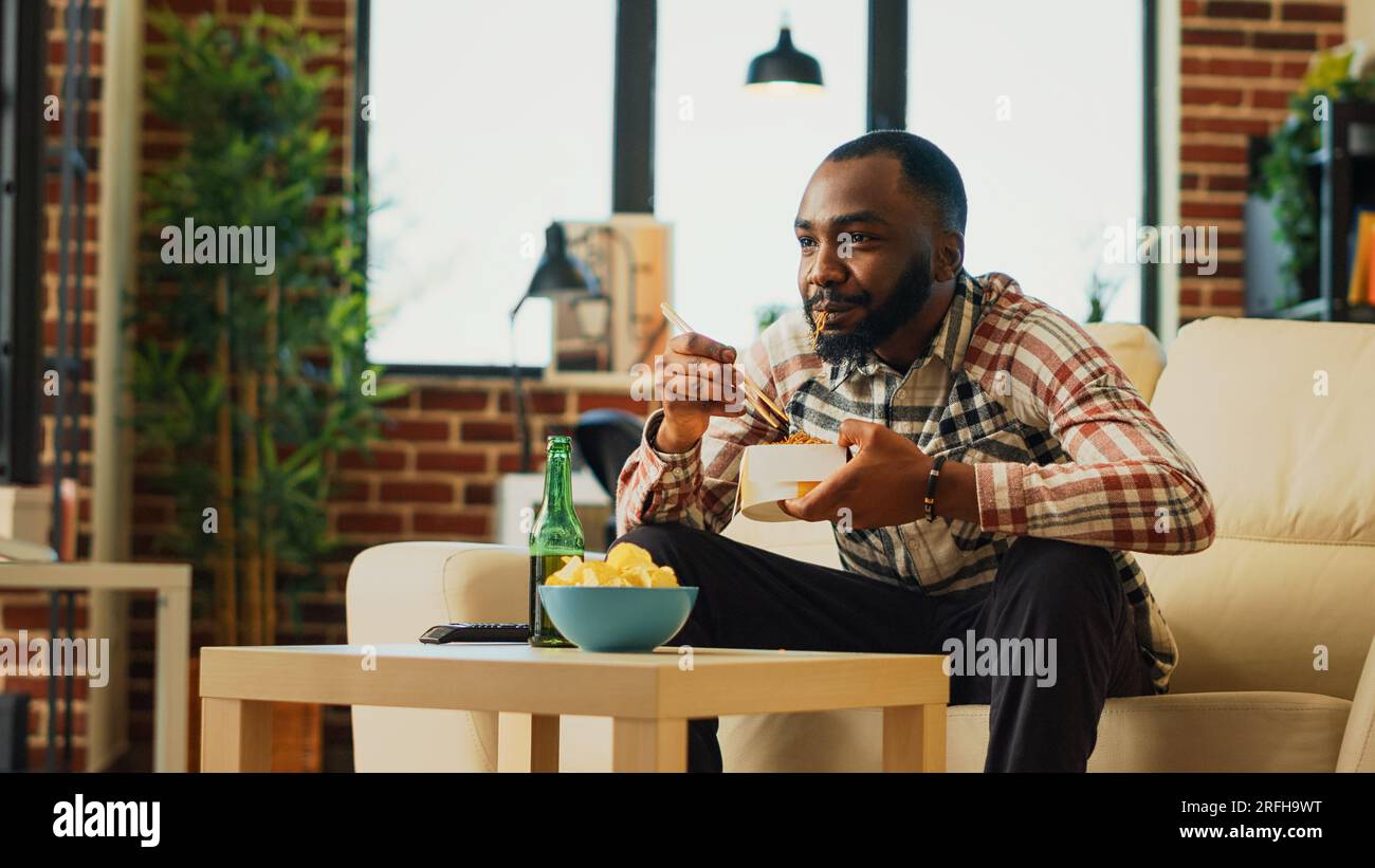 Happy guy eating noodles with chopsticks at home, enjoying asian food ...
