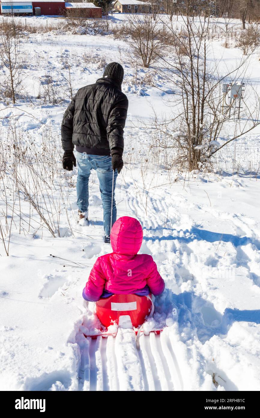 A man pulls his young daughter on her sled on a cold winter day at ...