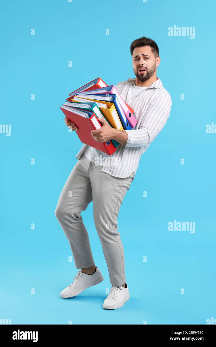 Stressful man with folders walking on light blue background Stock Photo ...