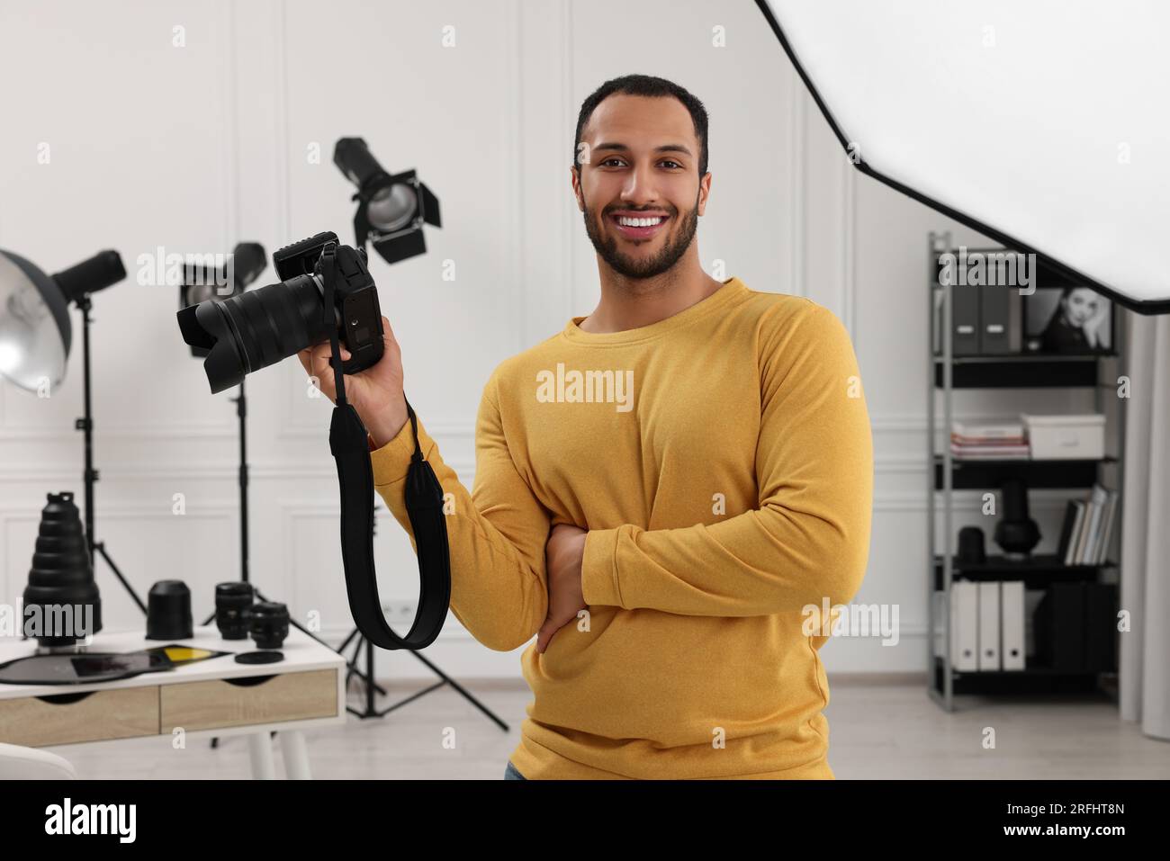 Young professional photographer with camera in modern photo studio ...