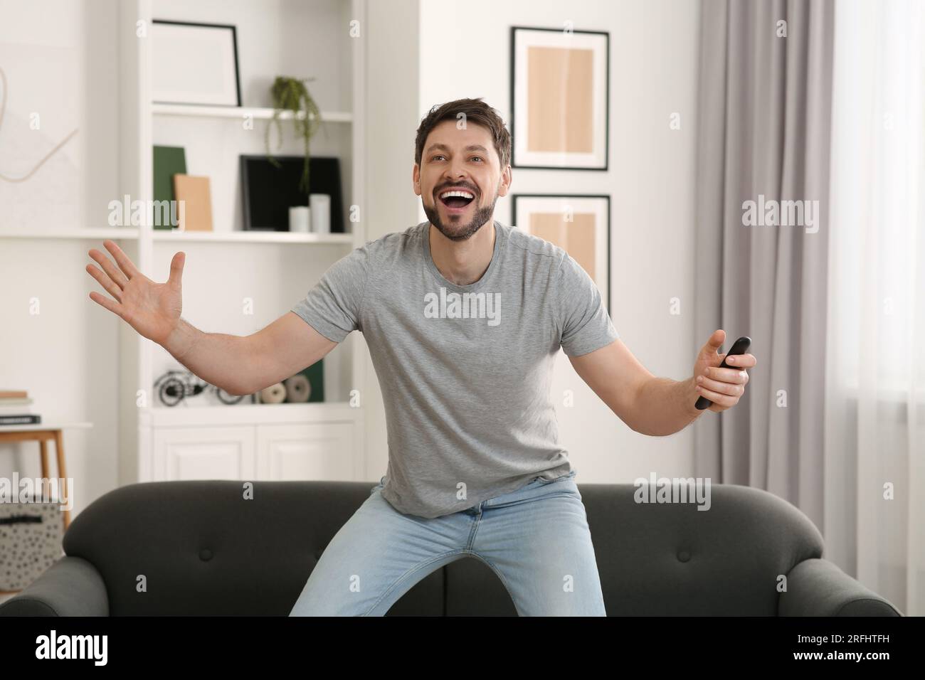 Emotional man holding remote controller and watching TV at home Stock ...