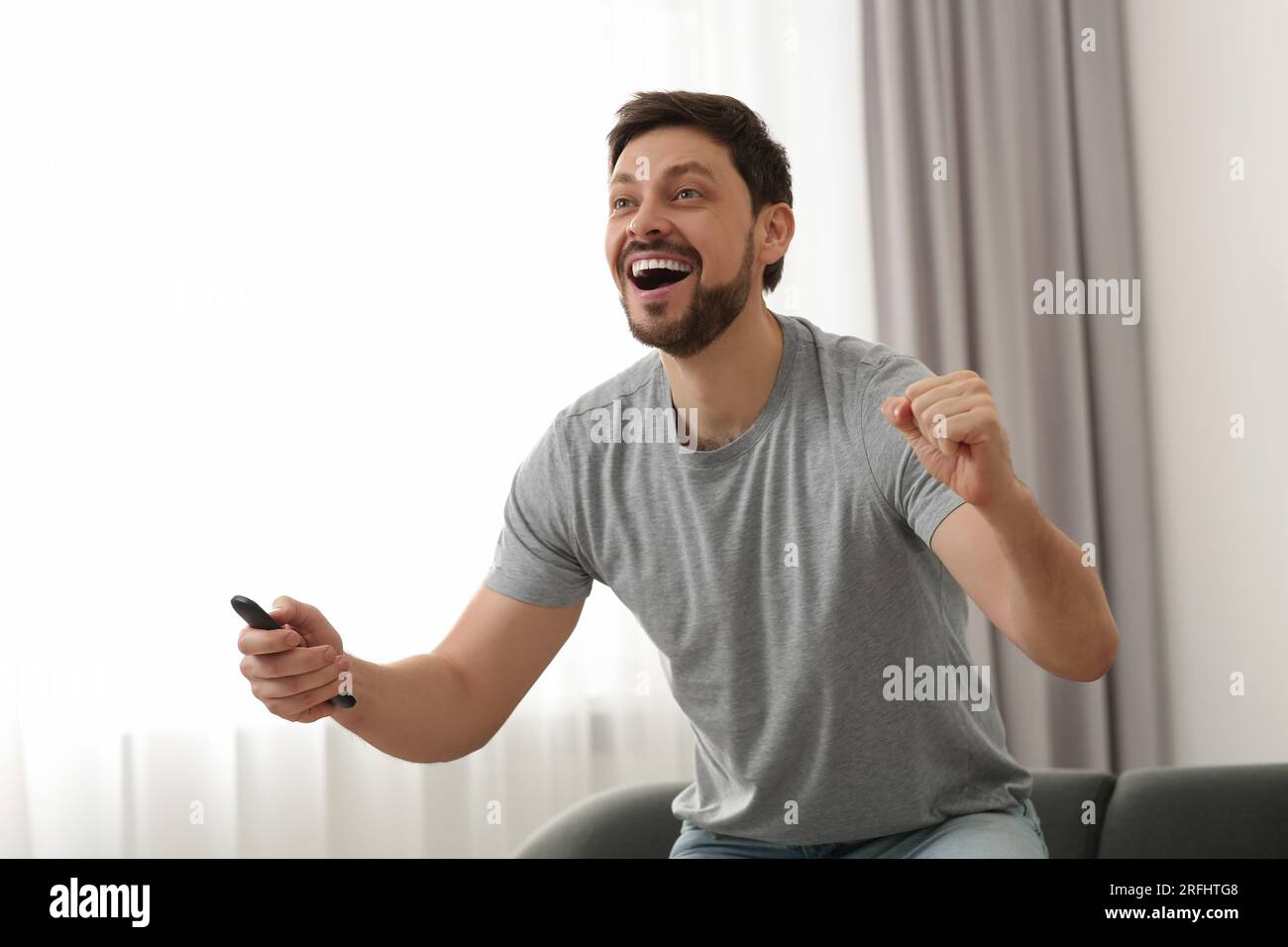 Emotional man holding remote controller and watching TV at home Stock ...