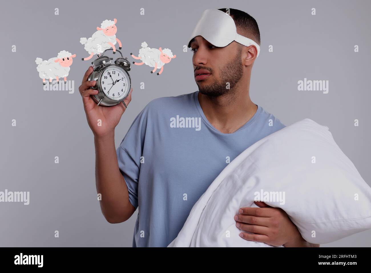 Insomnia. Tired man with pillow checking time on light grey background ...