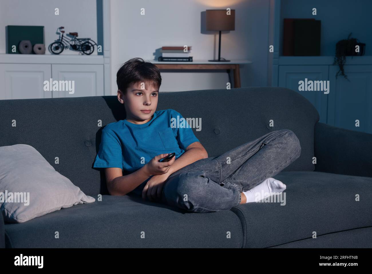 Little boy changing TV channels with remote control on sofa at home ...