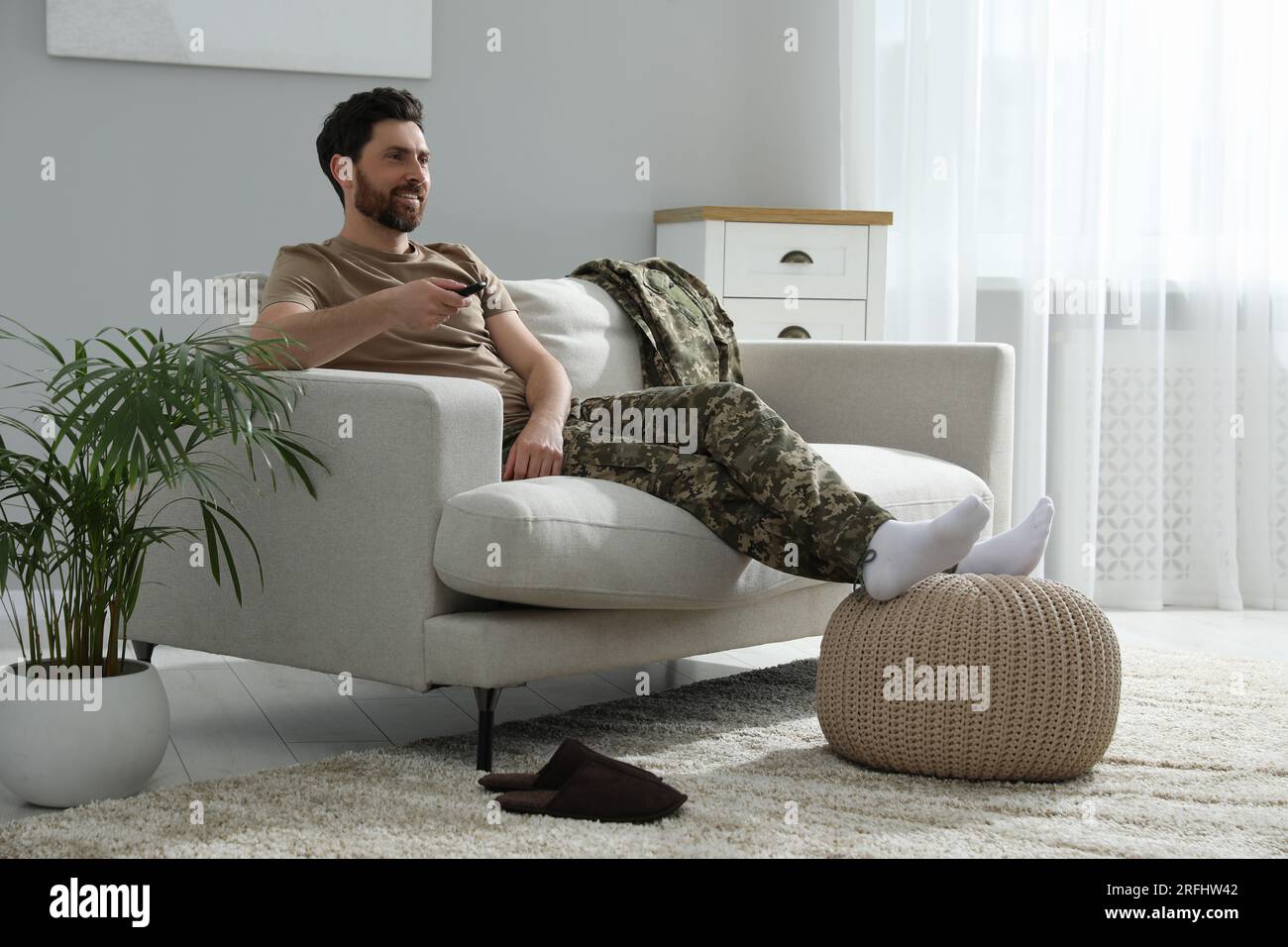 Happy soldier watching TV on sofa in living room. Military service ...