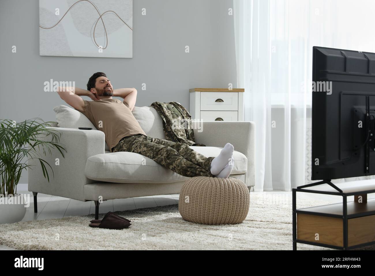 Soldier napping on soft sofa near TV in living room. Military service ...