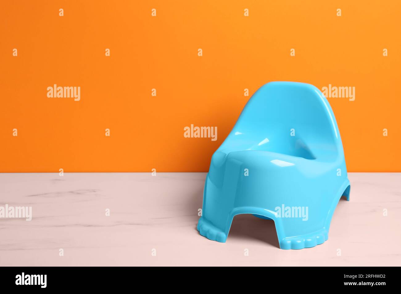 Light blue baby potty on white marble table against orange background ...