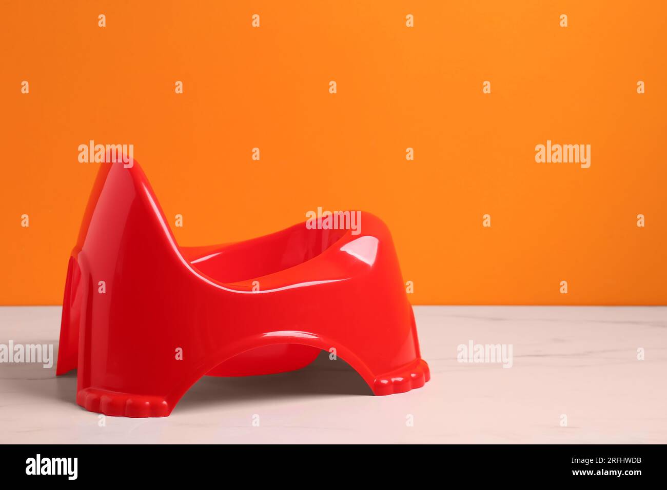 Red baby potty on white marble table against orange background, space ...