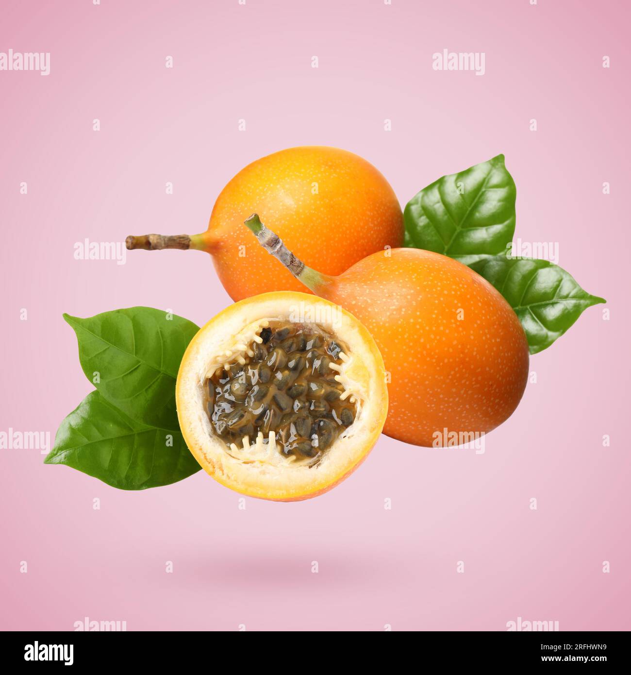 Delicious ripe granadillas with green leaves falling on pink background ...