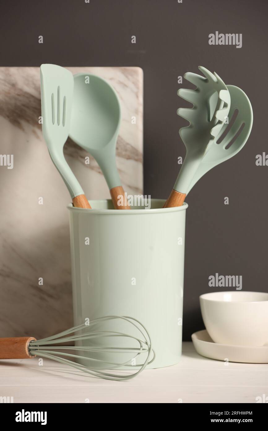 Set of different kitchen utensils on white wooden table against grey ...