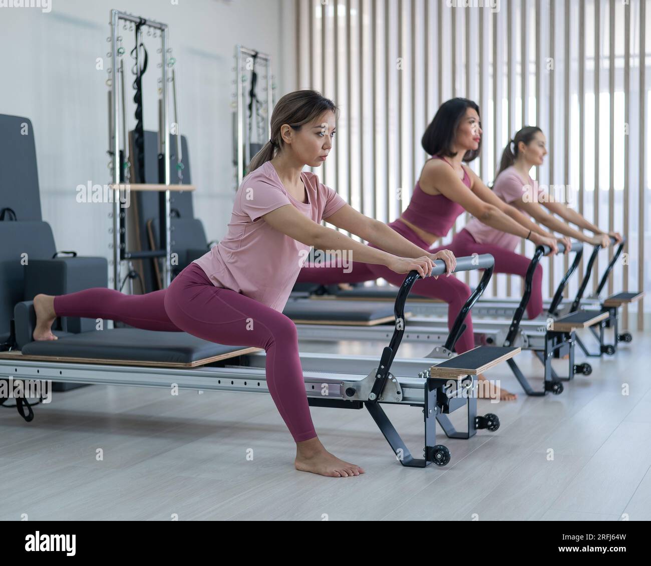 Three Asian women doing lunges on a reformer machine Stock Photo - Alamy