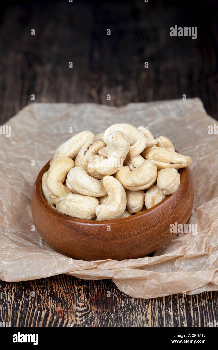 dry cashew nuts on an old wooden table and in a wooden bowl, a pile of ...