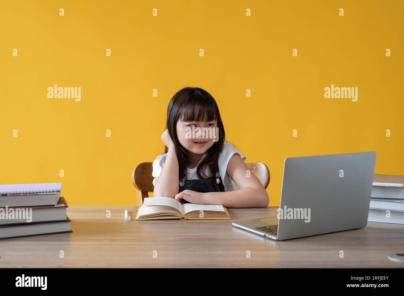 A happy, cute young Asian girl studies an online lesson on a laptop at ...