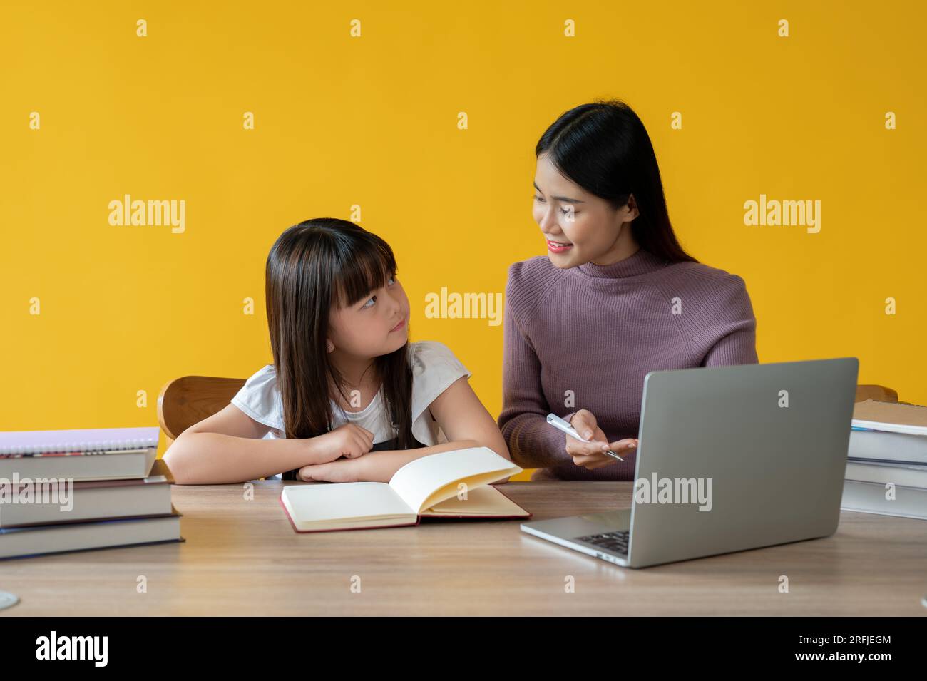 An adorable young Asian girl is studying with a female tutor, sitting ...