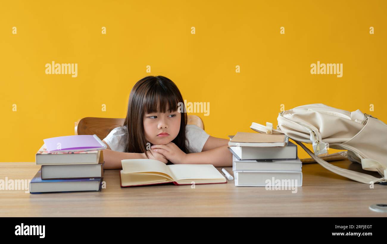 An adorable young Asian girl sitting at her study table with a bored ...