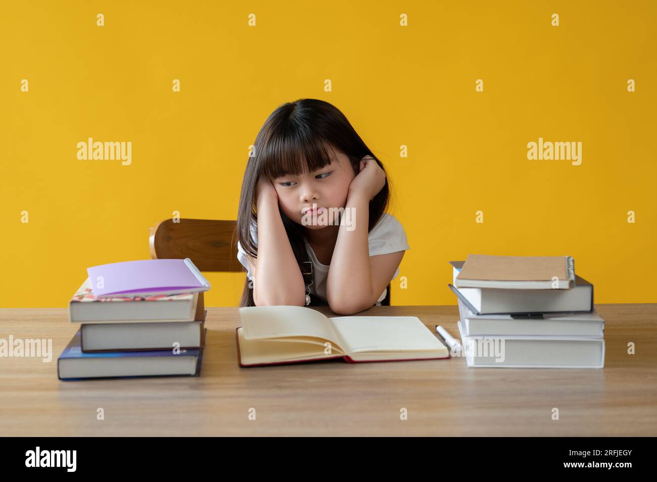 A cute young Asian girl sitting at her study table with a bored face ...