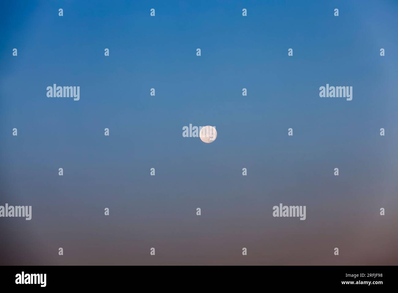 the moon shining in the still blue sky and reflecting the sunlight ...