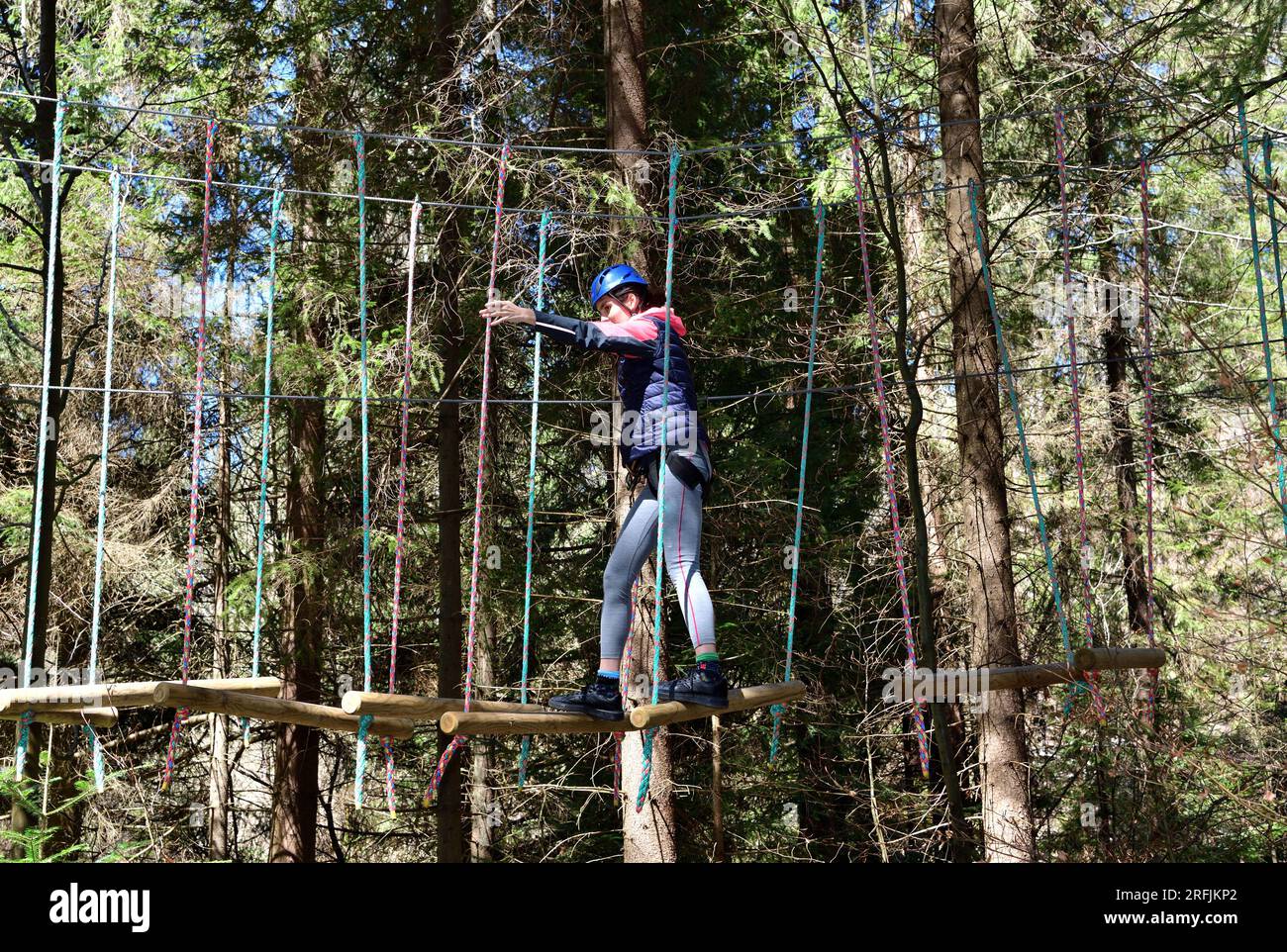 Young woman overcomes wooden obstacles at heights holding on to a rope ...
