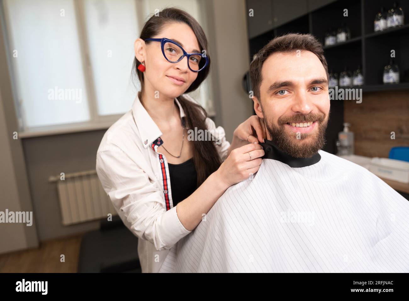 Pretty woman in earring putting on protective cape to smiling man Stock ...