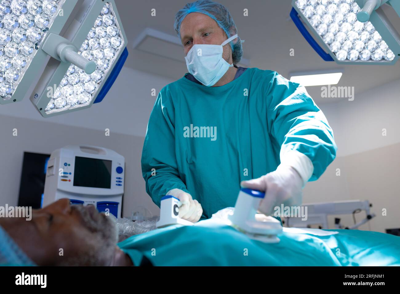 Caucasian male surgeon using defibrillators on african american patient ...