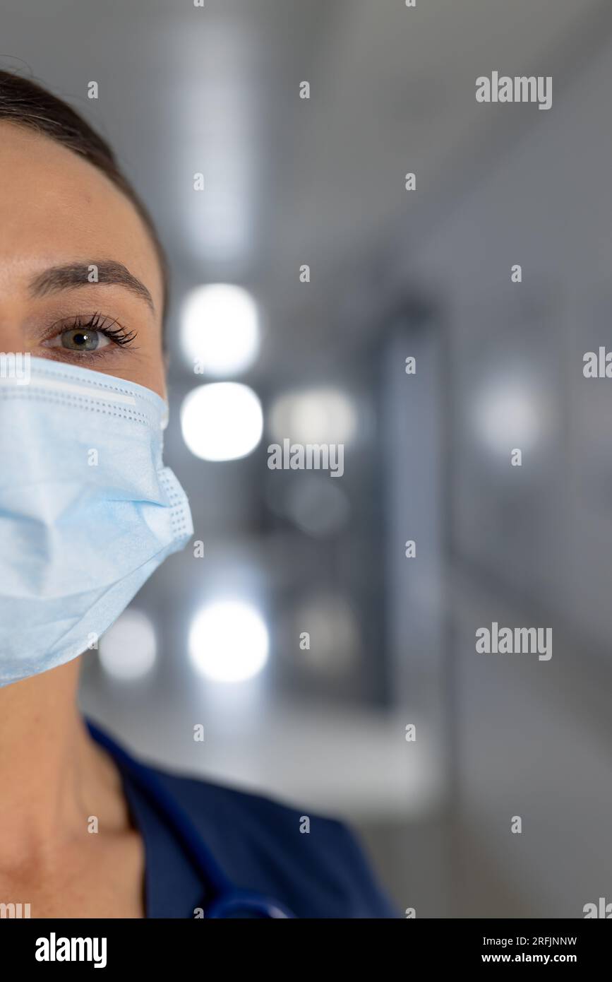 Portrait of caucasian female doctor wearing face mask in corridor at ...