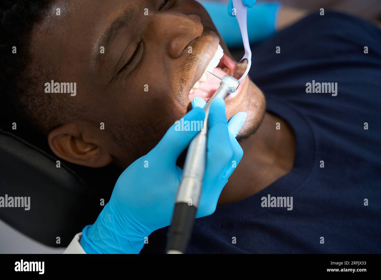 Female dentist looking at mouth mirror and working with dental drill to ...
