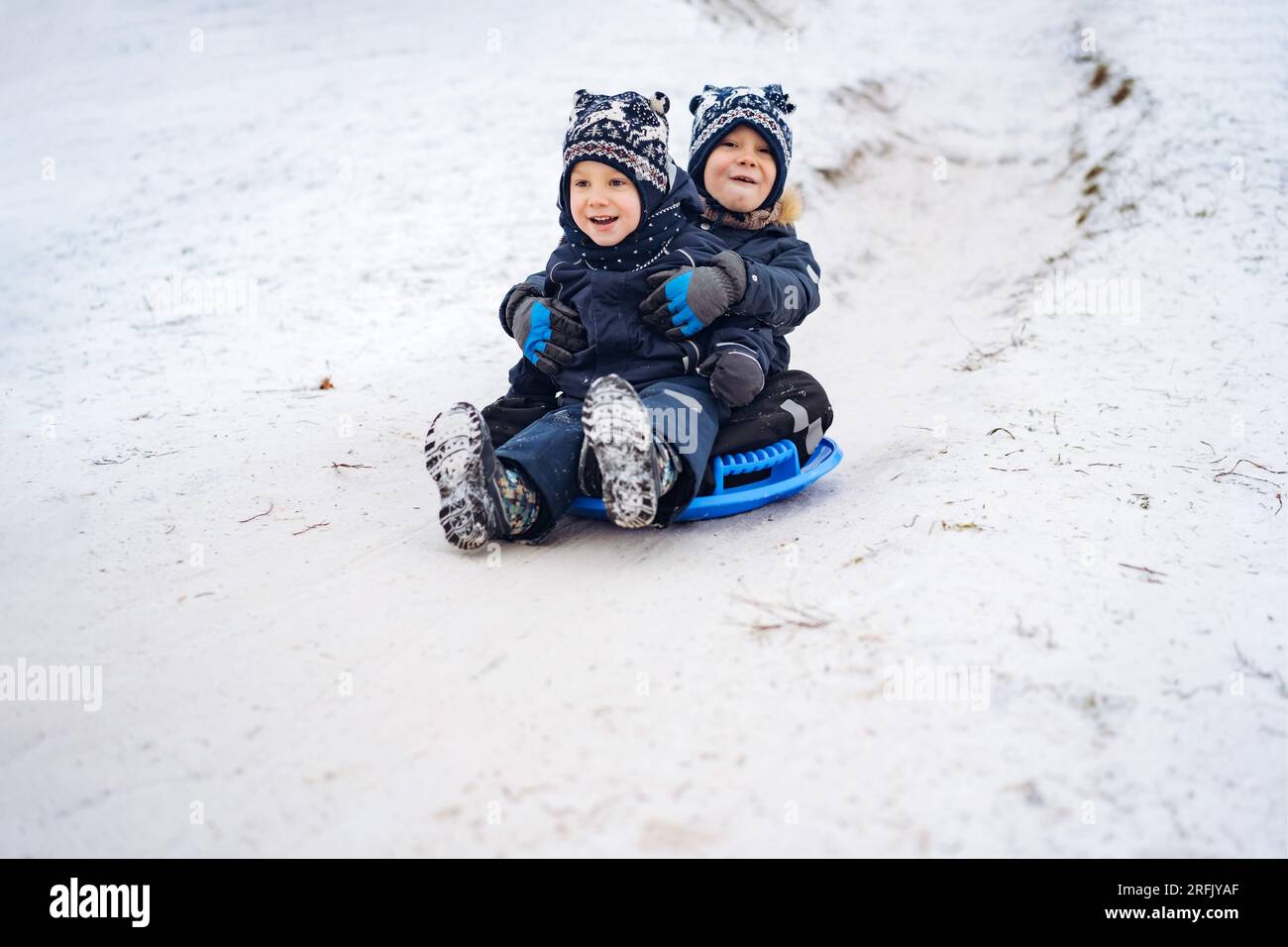 cute caucasian boys sliding down the icy slope in park . Winter ...