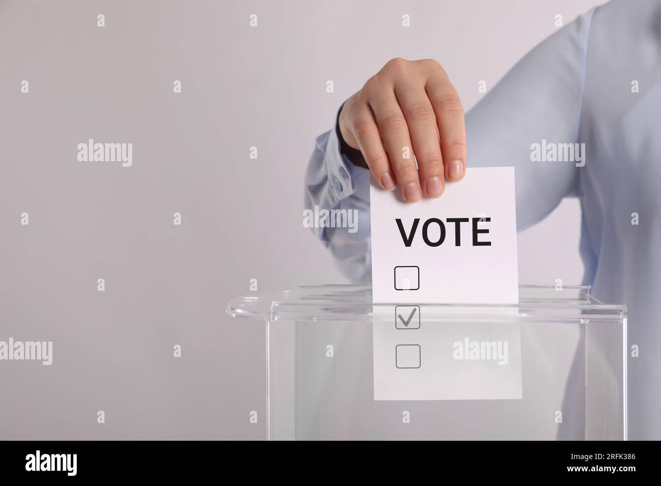 Woman putting paper with word Vote and tick into ballot box on light ...