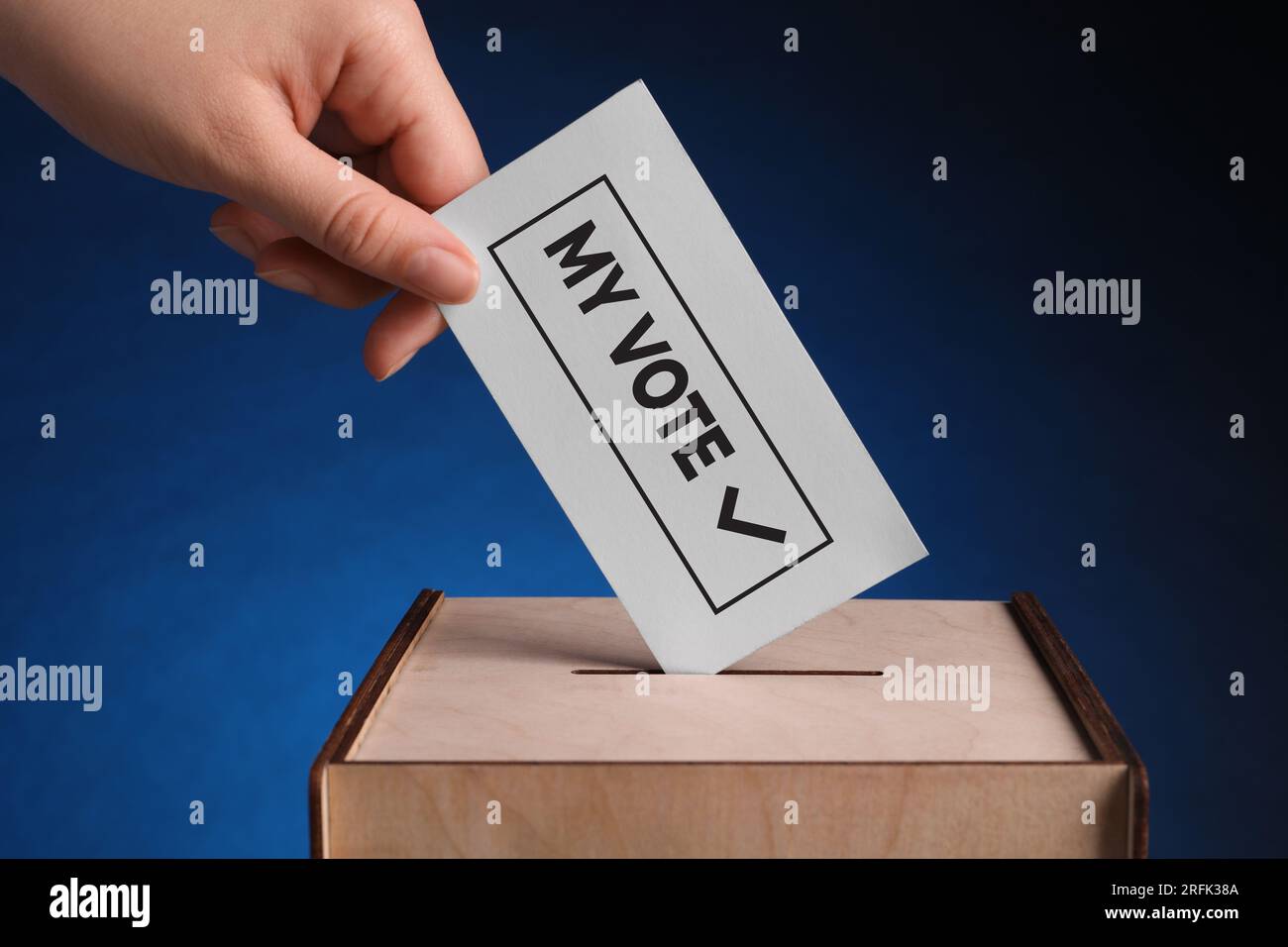 Woman putting paper with text My Vote and tick into ballot box on dark ...