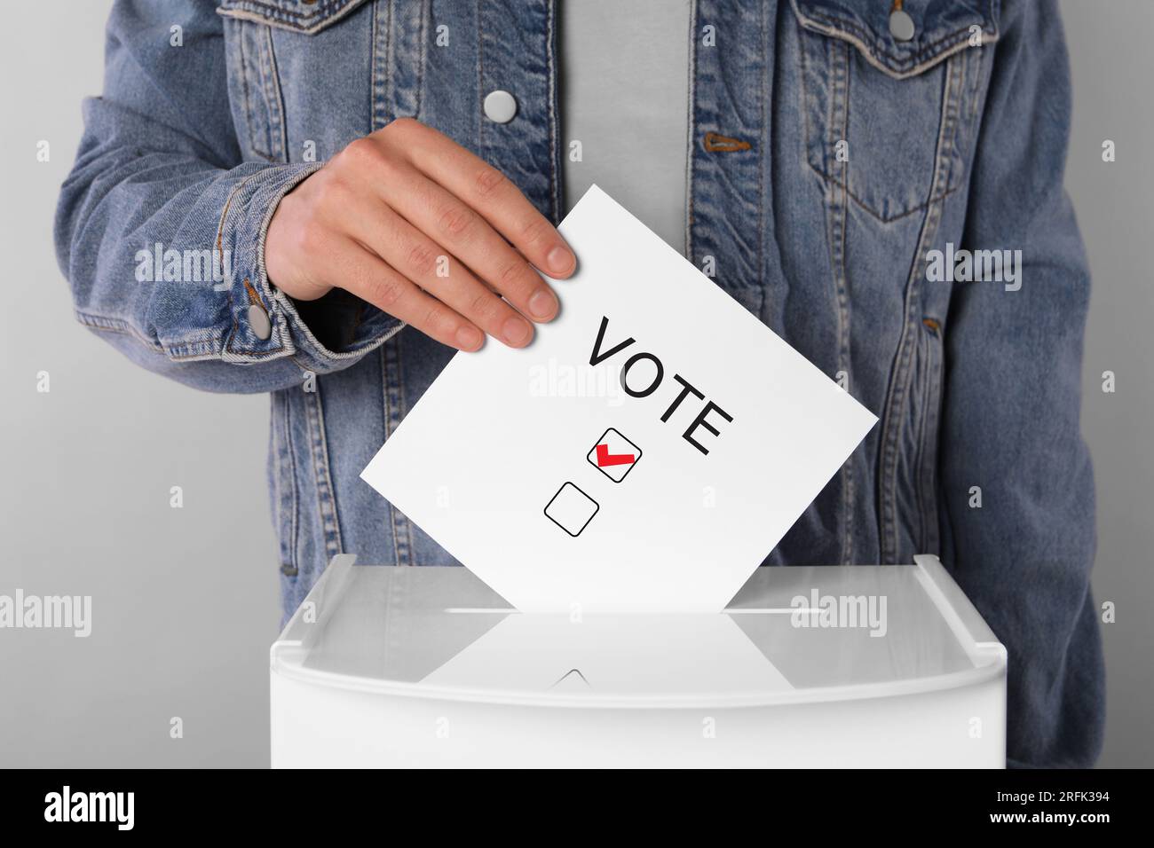 Man putting paper with word Vote and tick into ballot box on light grey ...