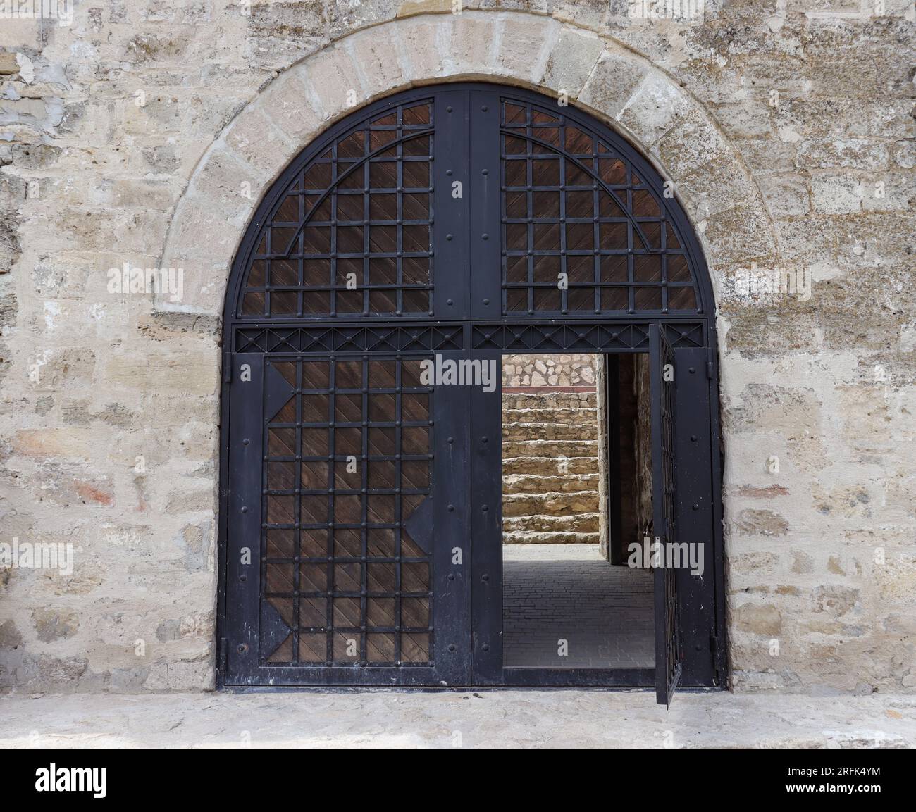 Black iron open gate in a stone wall, entrance into a medieval fortress ...