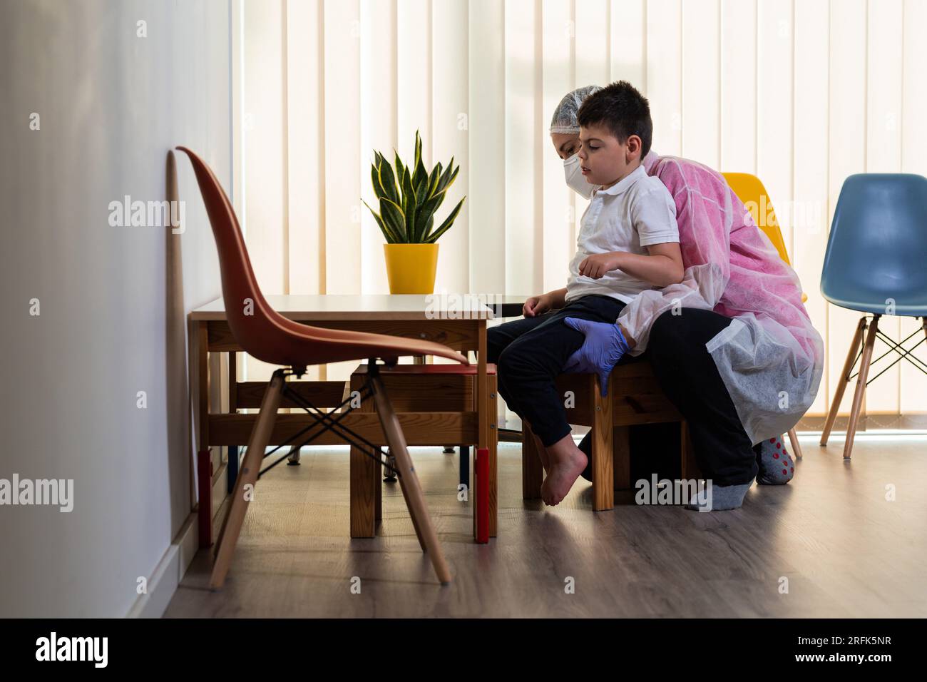 disabled child is being seated in a chair by a physiotherapist in front ...
